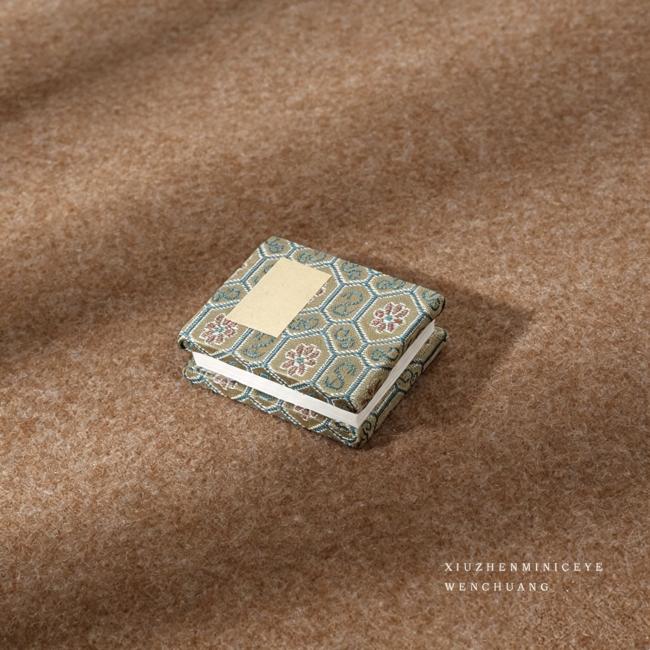 Front view of a mini hardcover accordion notebook wrapped in brown traditional Chinese brocade fabric featuring an affixed blank label panel