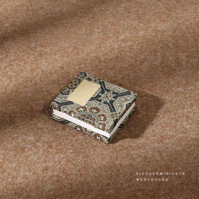 Close-up presentation of a mini brocade accordion notebook with a geometric hexagonal pattern and floral motifs