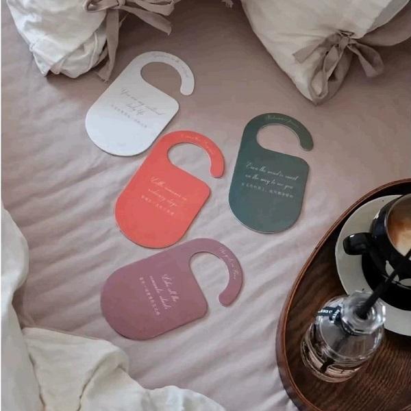 Flat lay presentation of four colored wardrobe fragrance cards featuring hanger cutouts and minimalist typography resting on a bed sheet