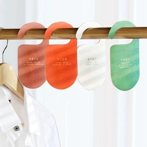 Application view of four diverse wardrobe fragrance cards hanging in a row on a wooden closet rail above a clean shirt