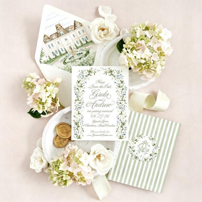 Flat lay of custom watercolor venue illustration wedding invitation card suite with botanical floral framing and matching envelope liner