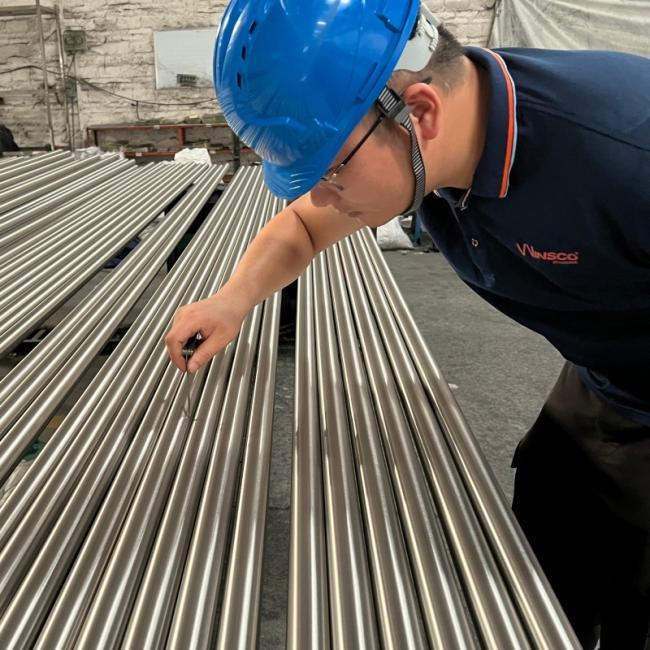 `VVINSCO factory worker inspecting polished stainless steel round tubes before shipment, quality control`