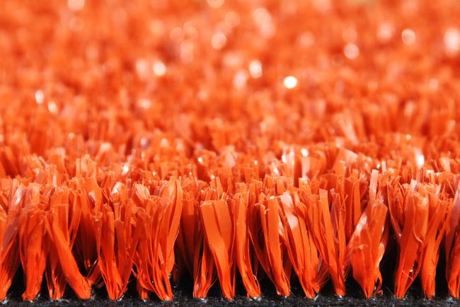 Close-up view of orange artificial turf fibers and backing structure