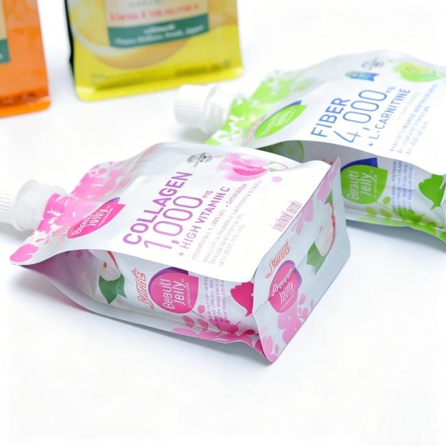Top-down close-up shot of pink collagen jelly spout pouch and green fiber L-carnitine drink stand up pouch, glossy transparent food grade laminated packaging, custom floral & fruit pattern printing for wellness beauty drinks.