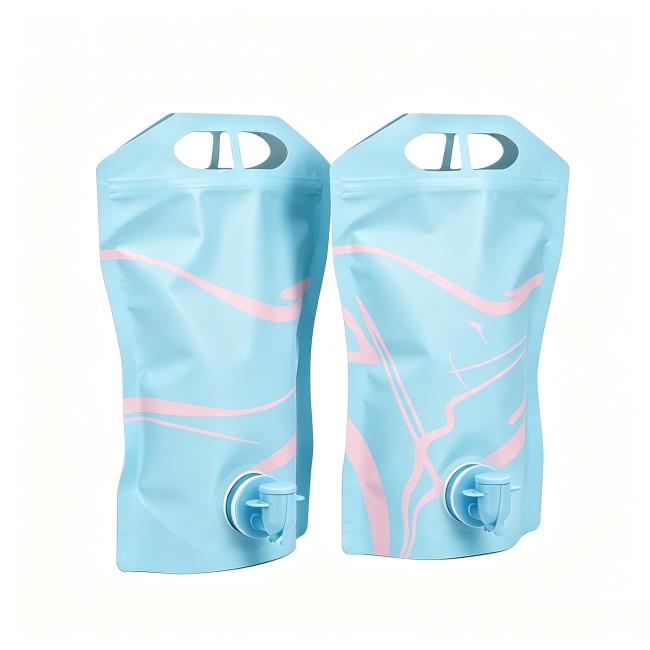 Studio flat lay display of two identical light blue wine bib pouches with pink abstract graphic printing. Both feature dual die-cut top handles, upper resealable zipper, bottom blue flip tap valve, showing consistent finished product appearance for bulk wholesale packaging portfolio.