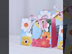 Premium-Geschenktüte mit Blumenmuster und goldenen Kordelgriffen, schicke Schleife, lebendiges blaues, mehrfarbiges Blüten-Design