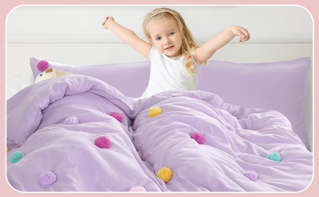 Purple pom-pom toddler bedding set displayed on a bed